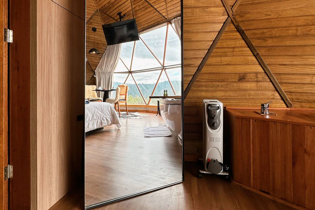 Quarto com teto de madeira, uma cama, uma cadeira, uma mesa e um aquecedor.