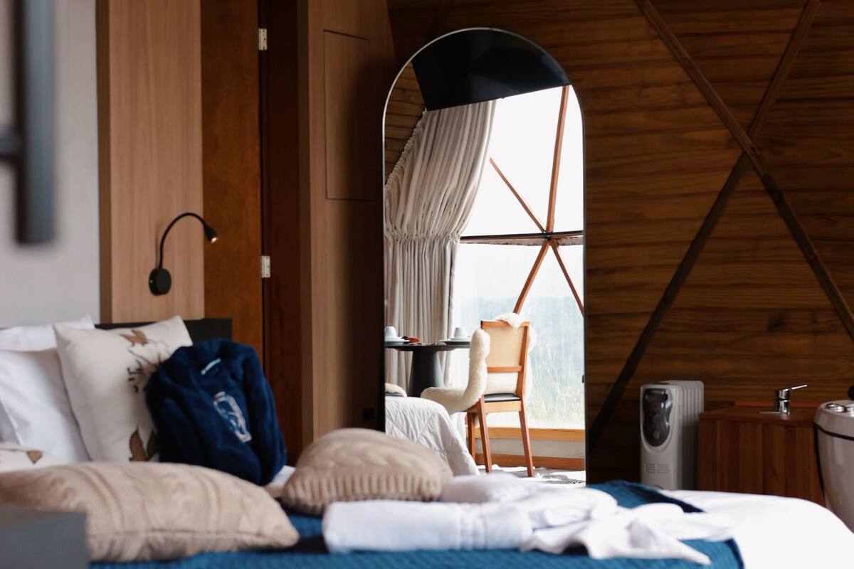 Quarto com cama, escrivaninha, cadeira e janela com cortinas.