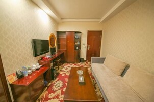 Quarto de hotel com sofá, uma mesinha, televisão na parede e um armário de madeira com espelho.