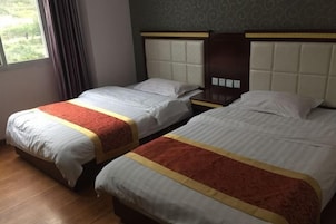 Duas camas de solteiro com cabeceiras, uma janela com cortinas e uma parede com padrão.