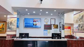 Uma área de recepção de hotel com balcão de mármore, visor digital e certificados emoldurados na parede.