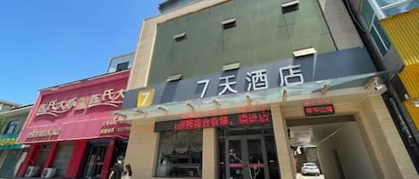 Um edifício com uma placa que diz '7天酒店', indicando um hotel. Há uma fachada com toldo vermelho e uma placa que diz '餐厅', que significa restaurante.