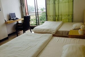 Quarto de hotel com duas camas, uma escrivaninha com computador e vista para o verde pela janela.