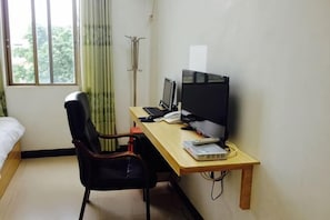 Um quarto com cama, escrivaninha com computador, cadeira e janela com cortinas.