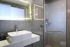 Casa de banho moderna com chuveiro em cabine de vidro, lavatório branco e espelho com iluminação embutida.