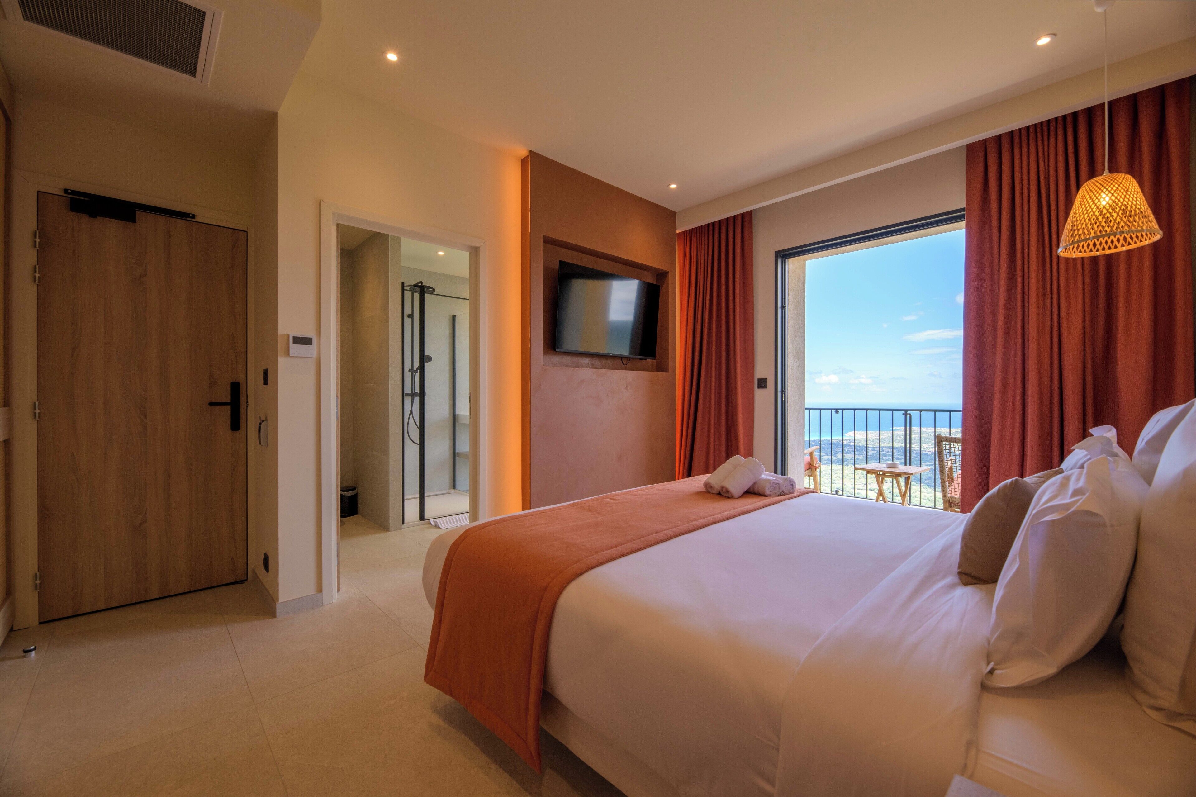 Quarto de hotel com uma cama grande, televisão na parede, varanda com vista e porta de madeira.