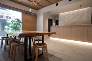 Uma área de recepção moderna, com um balcão de madeira, uma mesa grande com bancos e vista para o verde lá fora.