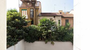 Edifício residencial com varanda, parede branca e vegetação densa na frente.