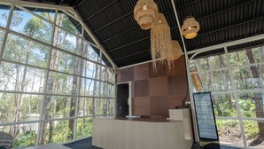 Uma receção com design moderno, grandes janelas com vista para a floresta e luminárias pendentes.