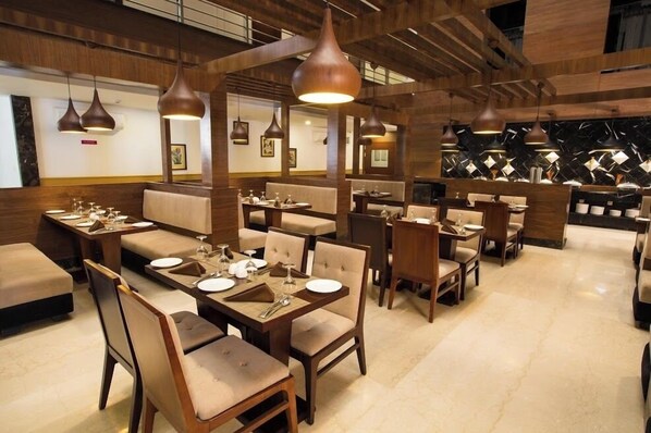 Restaurante com vigas de madeira no teto, iluminação pendente e uma combinação de assentos em camarotes e mesas.
