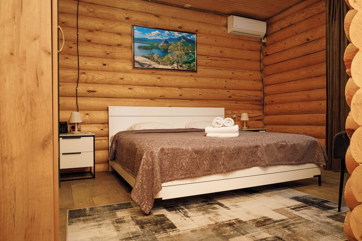 Quarto de cabana de madeira com cama, abajures, um quadro e parede de toras.