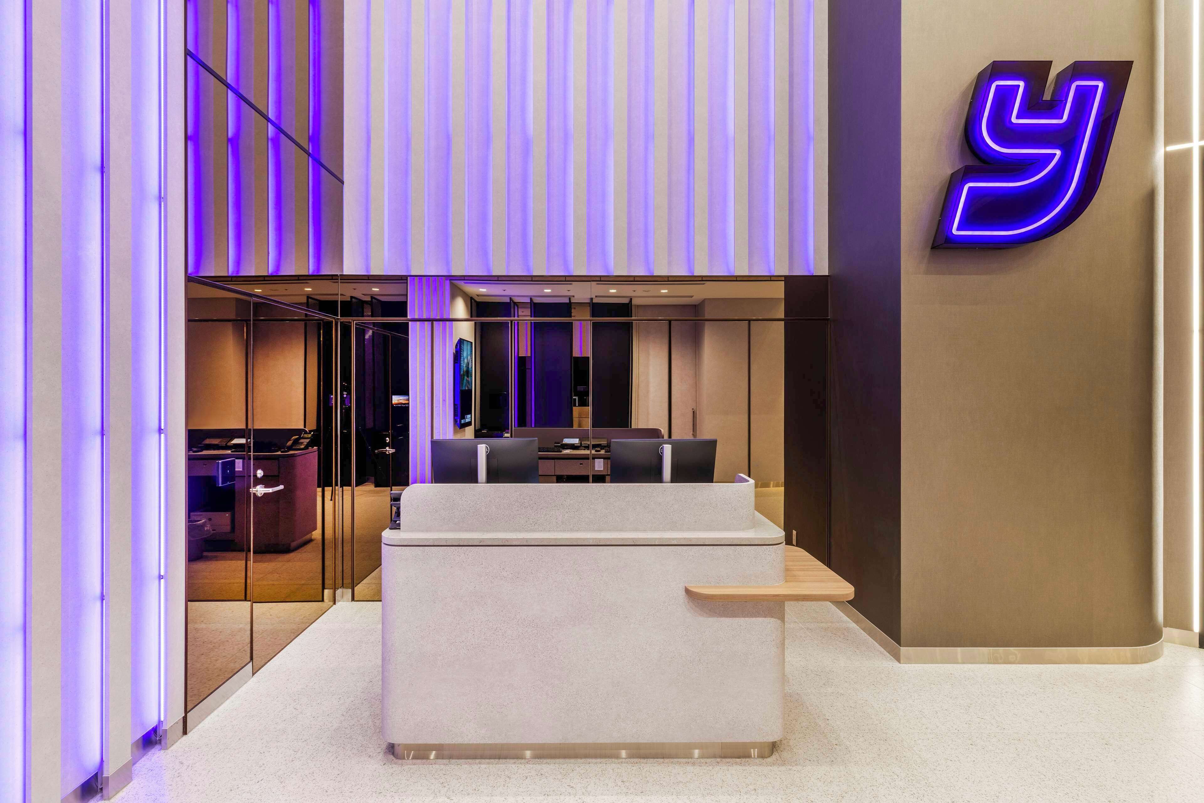 Uma área de recepção com design moderno, com balcão de atendimento, espaço para sentar e um letreiro de neon.