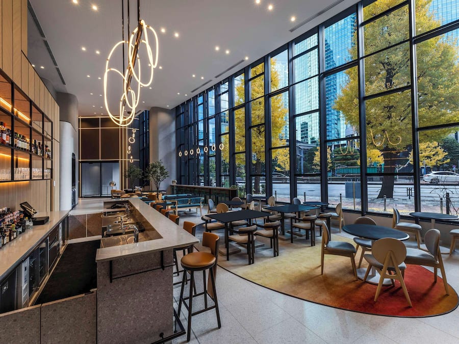 Uma área de bar moderna com balcão, banquetas e assentos. Janelas amplas oferecem vista para o exterior.