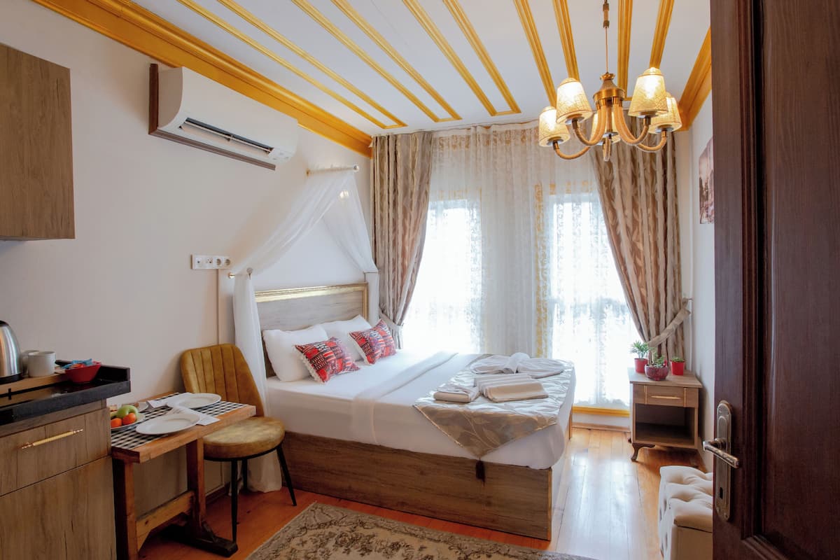 Quarto com cabeceira de madeira, cama com roupa de cama branca, mesa de cabeceira com abajur e janela com cortinas.