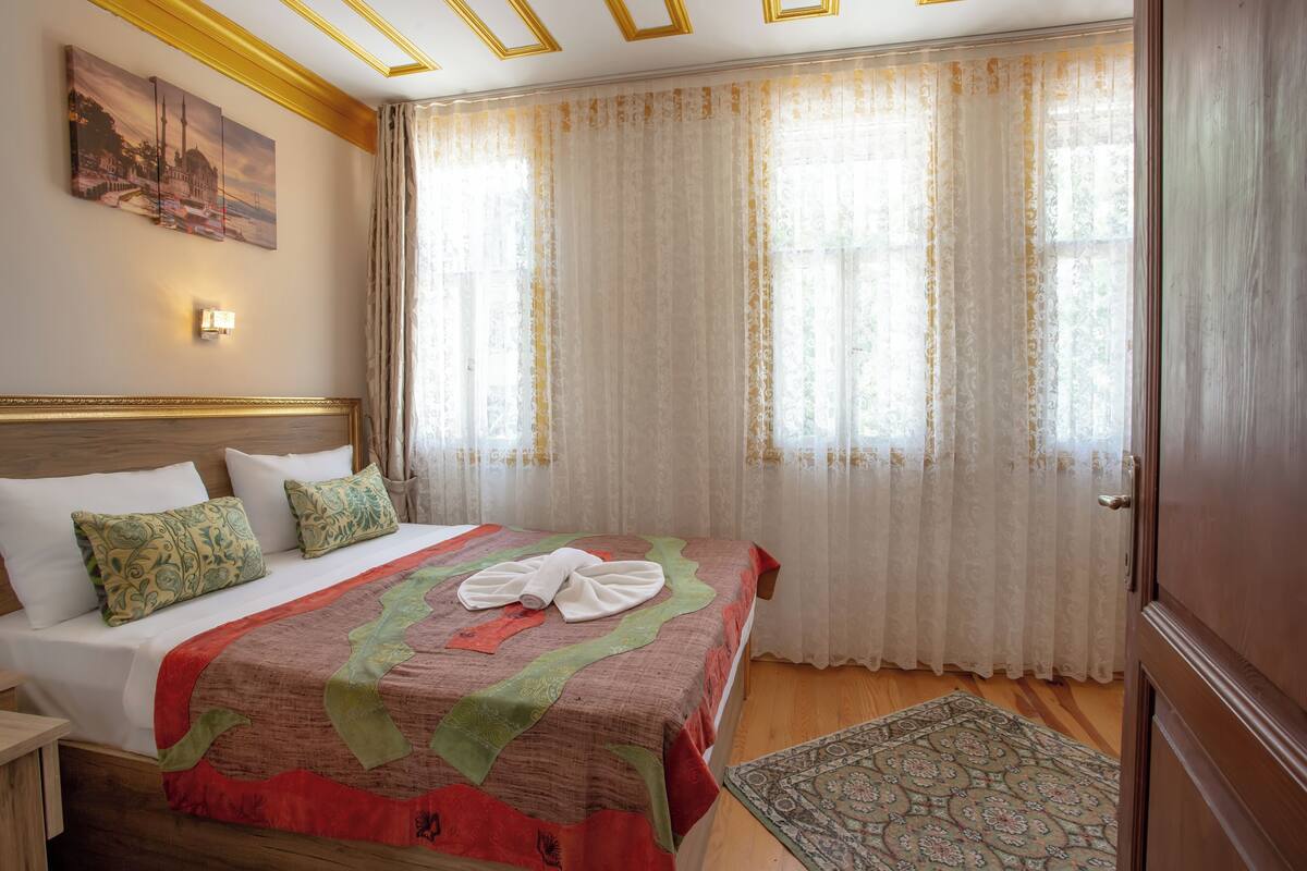 Cama bem arrumada com manta decorativa, cabeceira e luminária fixada na parede.