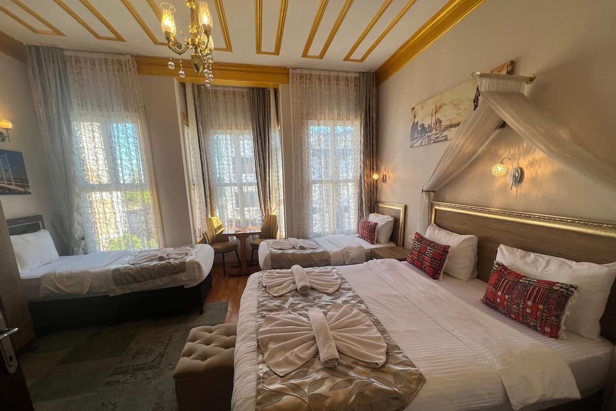 Quarto de hotel com duas camas de solteiro, uma cama de casal, uma mesa de jantar e um lustre.