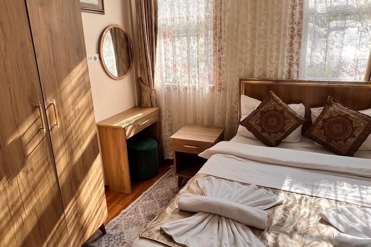Quarto com cama, guarda-roupa de madeira, escrivaninha e luminária pendente.