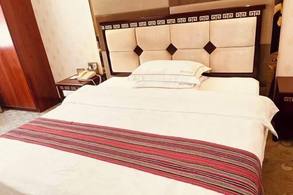 Quarto de hotel com uma cama, mesa de cabeceira com telefone e cabeceira com padrão geométrico.