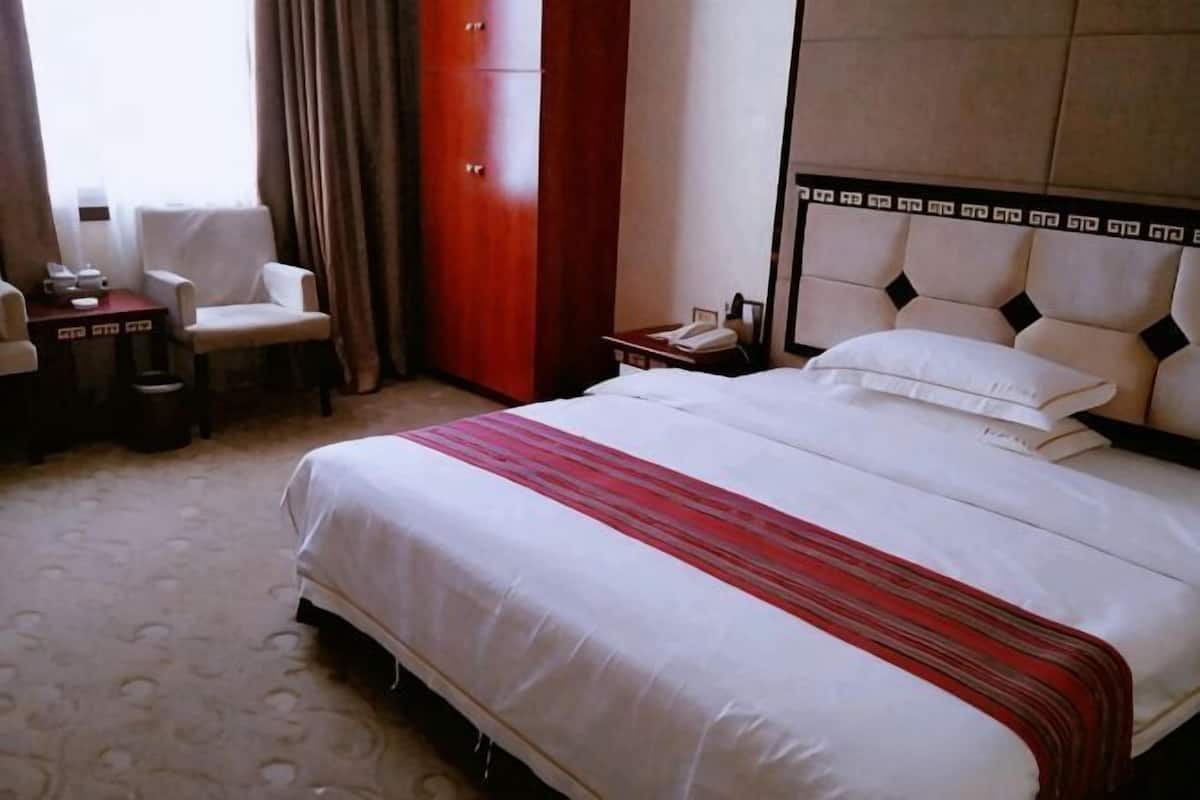 Quarto de hotel com cama, escrivaninha, cadeira, guarda-roupa e telefone.