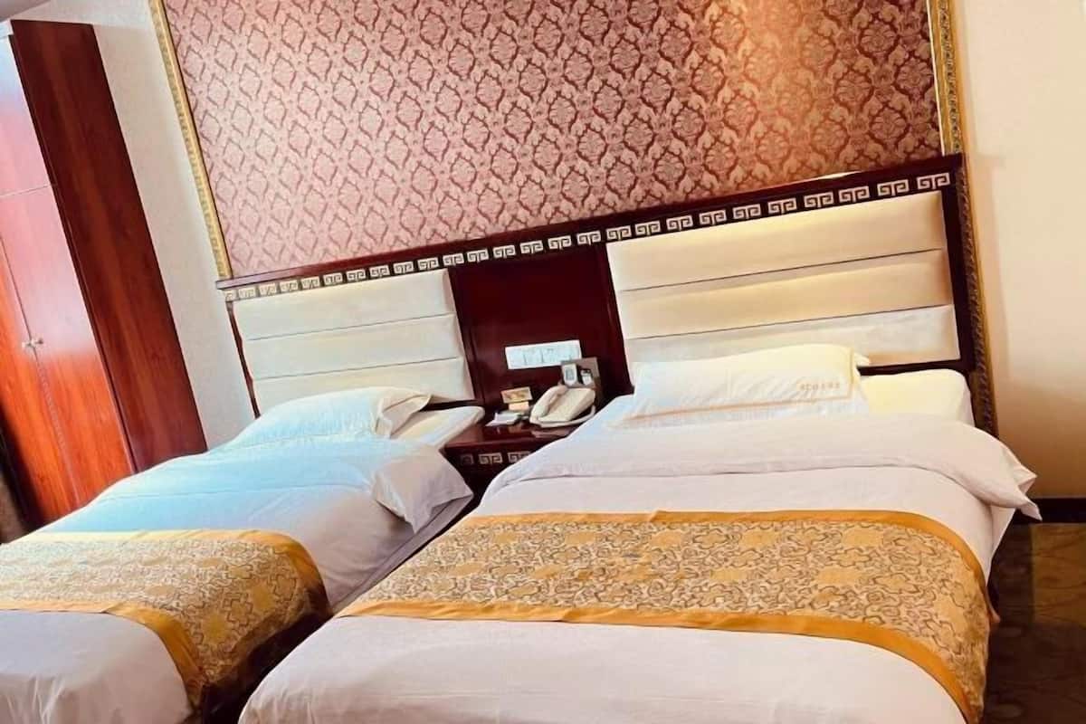 Quarto de hotel com duas camas, uma cabeceira de madeira, parede estampada e mesa de cabeceira com telefone.