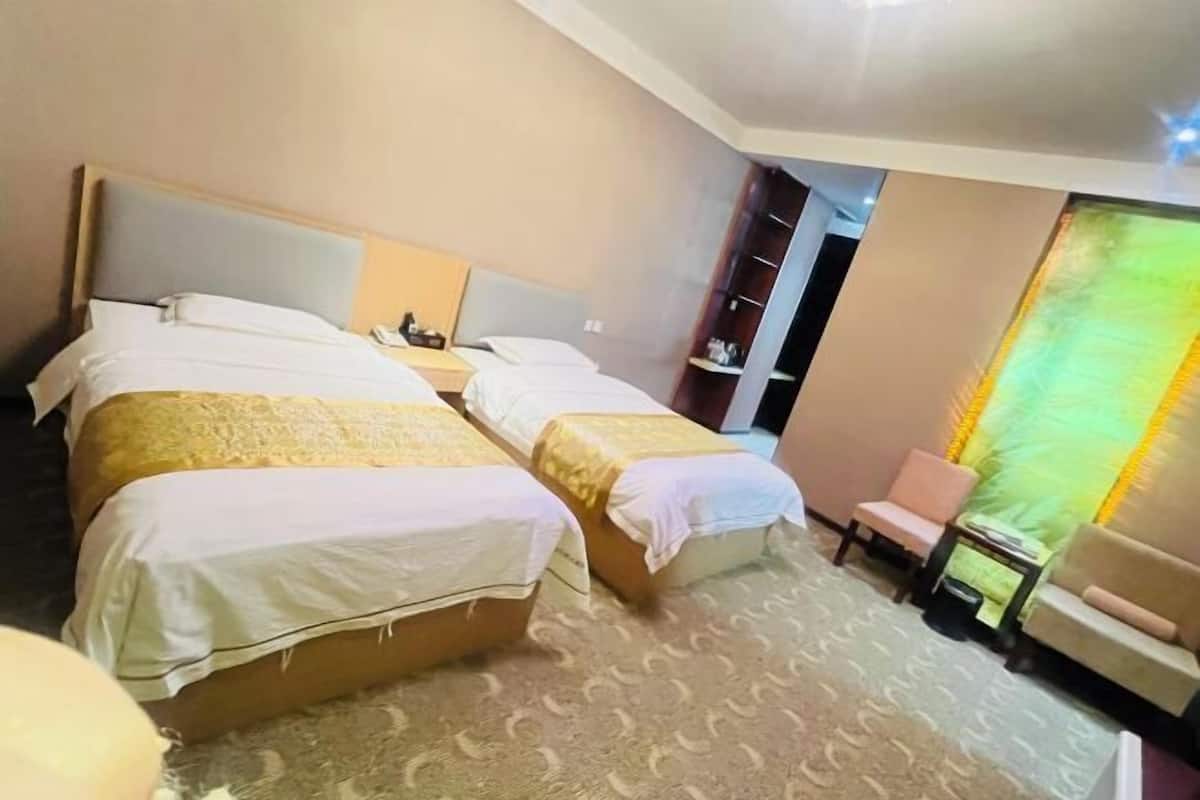 Quarto de hotel com duas camas, uma cadeira, uma mesinha e um guarda-roupa.