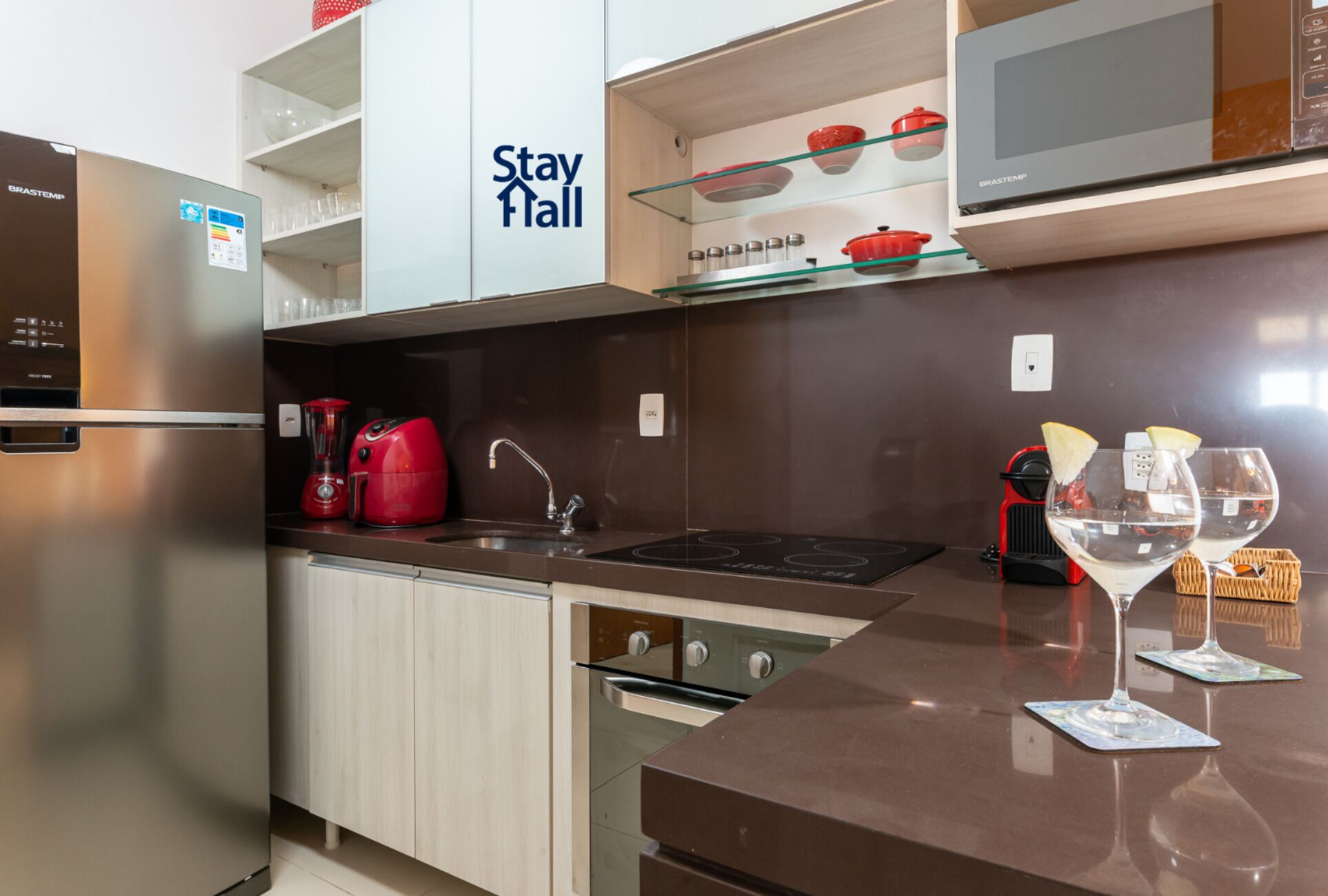 Cozinha moderna com frigorífico, fogão e micro-ondas. Há um letreiro na parede escrito 'Stay Hall'.