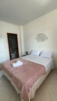 Quarto com cama, toalha, mesa de cabeceira, abajur e arte de parede com peixes.