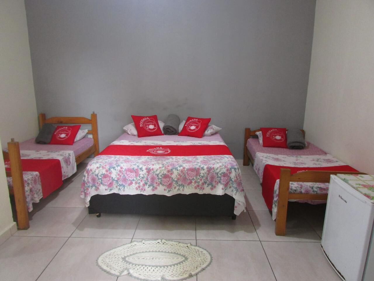 Quarto pequeno e compacto com uma cama de solteiro, duas mesas de cabeceira e um frigorífico pequeno.