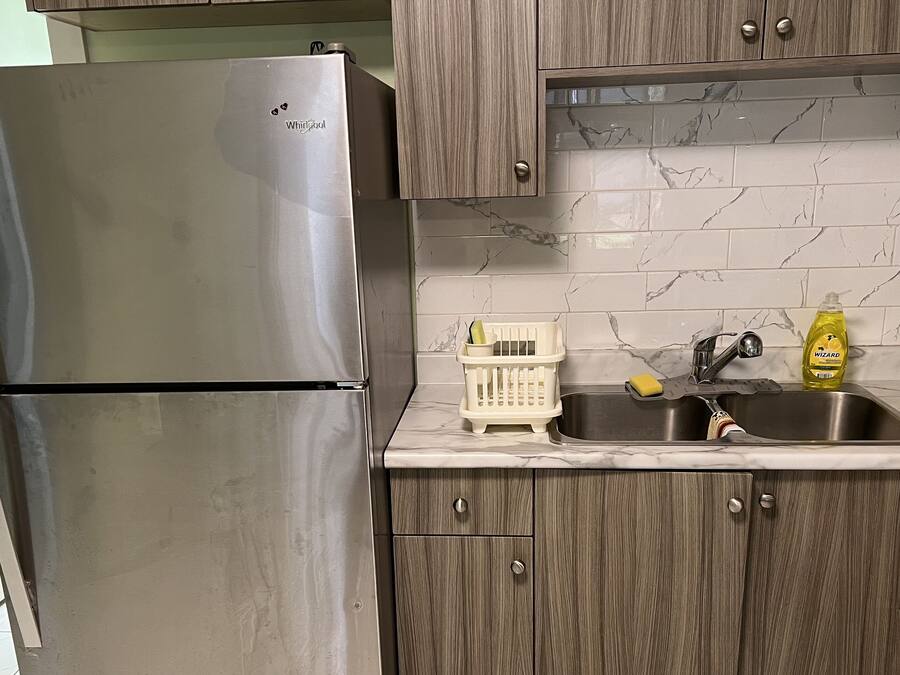 Cozinha com geladeira de aço inoxidável, armários de madeira, painel de fundo de mármore e pia com escorredor de louça.
