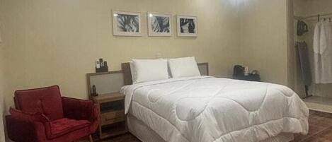 Quarto com uma cama grande, uma cadeira vermelha, uma mesinha de cabeceira e três quadros na parede.