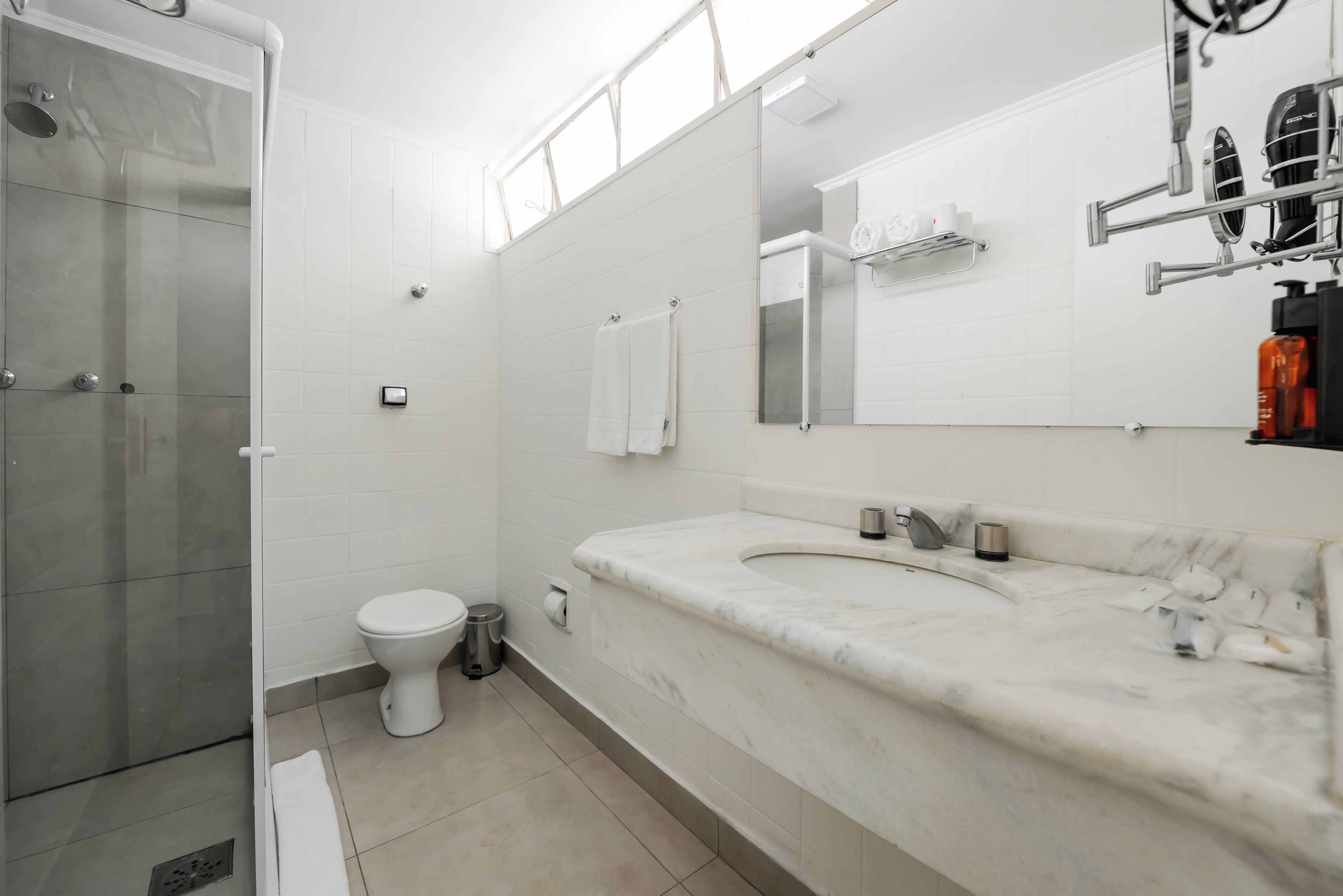 Um banheiro moderno com box de vidro, vaso sanitário e pia de mármore com espelho acima.