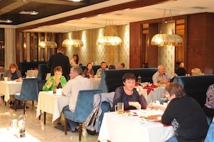 Restaurante com várias mesas e cabines, clientes a jantar e um garçom ao fundo.