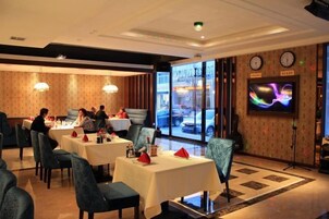 Restaurante com mesas preparadas para refeições, uma tela de televisão e vista para a rua.