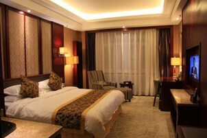 Quarto de hotel com uma cama grande, uma televisão, uma escrivaninha e uma cadeira.