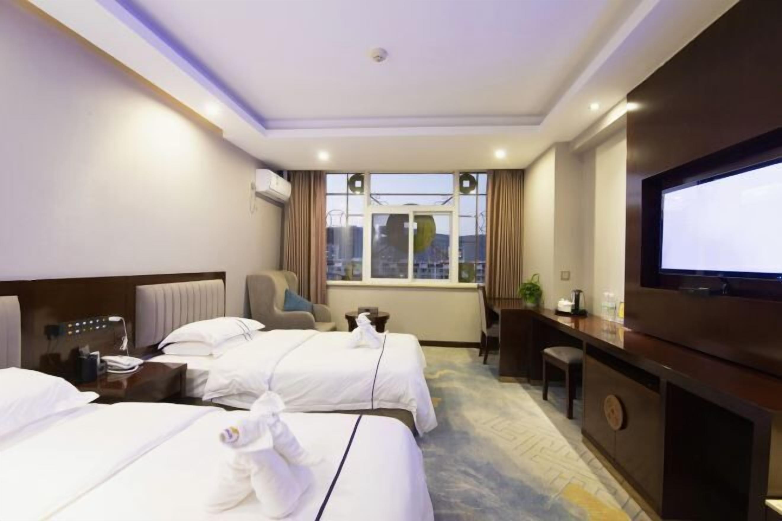 Quarto de hotel com duas camas, uma mesa, uma televisão e janela com vista para a cidade.