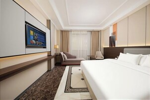 Quarto de hotel com cama, escrivaninha, cadeira, televisão e janela com cortinas.