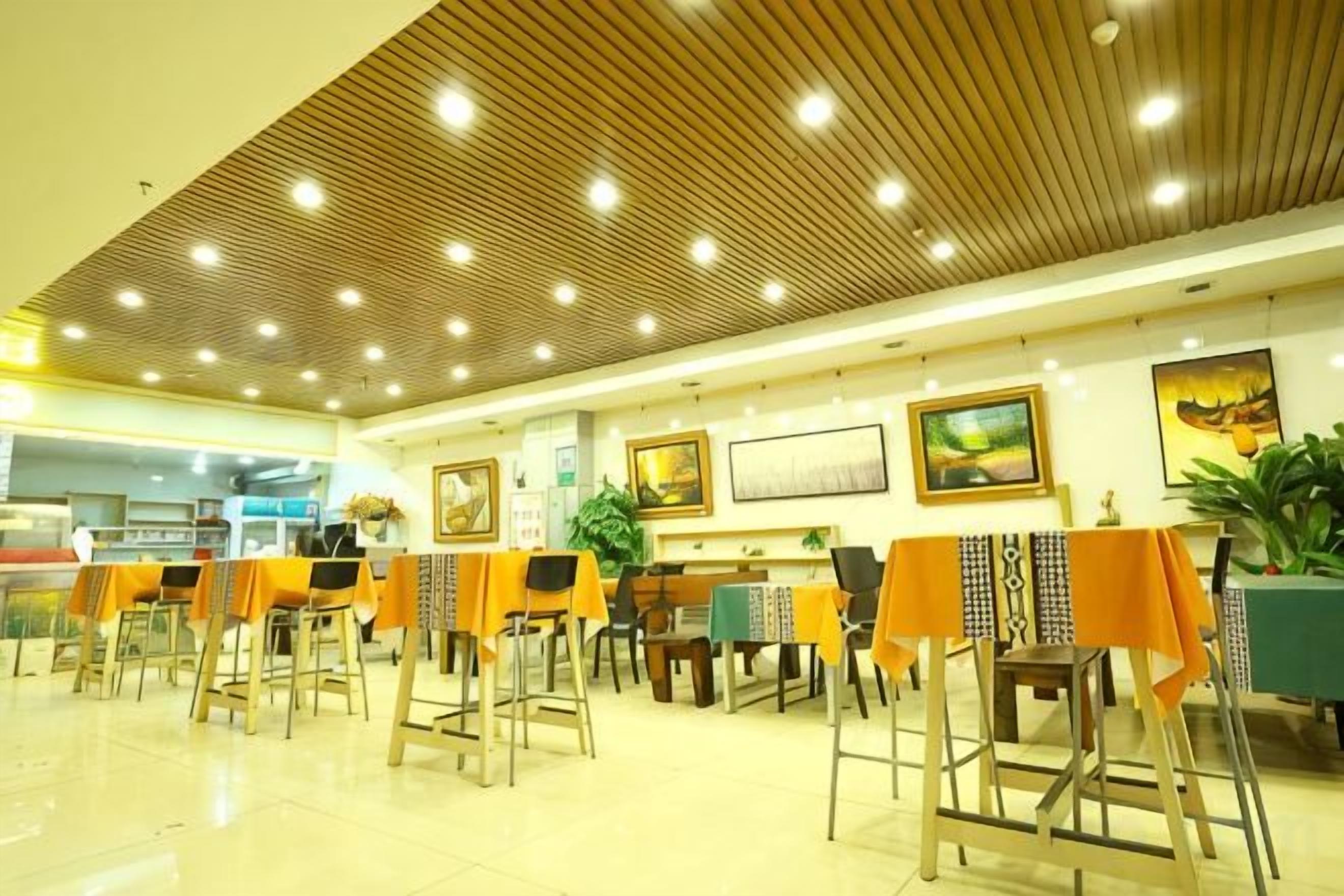 Restaurante com teto alto, várias mesas com toalhas laranja e chão de azulejos limpos.