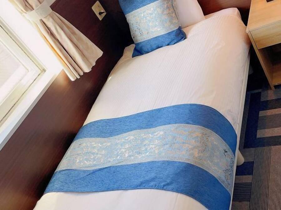 Uma cama com colcha e almofada azul e branca, um painel de cabeceira de madeira e uma janela com cortinas.
