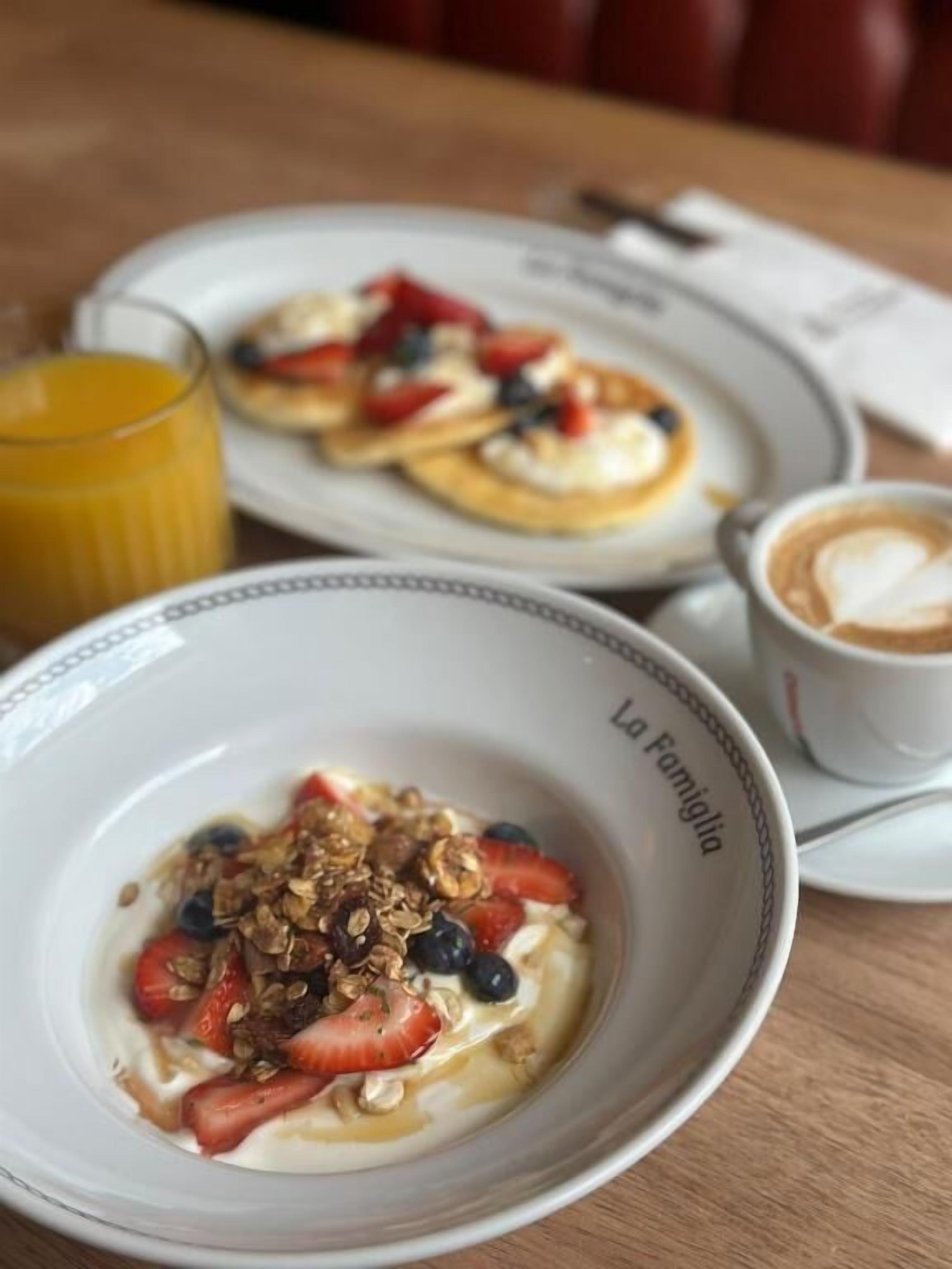 Uma mesa de café da manhã com pratos de comida, um copo de suco de laranja e uma xícara de café.