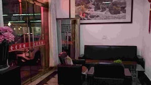 Quarto com sofá, uma mesa pequena, uma cadeira e um vaso decorativo. Há uma janela com vista para o exterior.