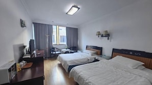 Quarto de hotel com duas camas, uma escrivaninha, uma cadeira, uma televisão e uma janela com cortinas.