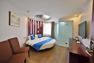 Quarto de hotel com cama, escrivaninha, cadeira, televisão e porta.