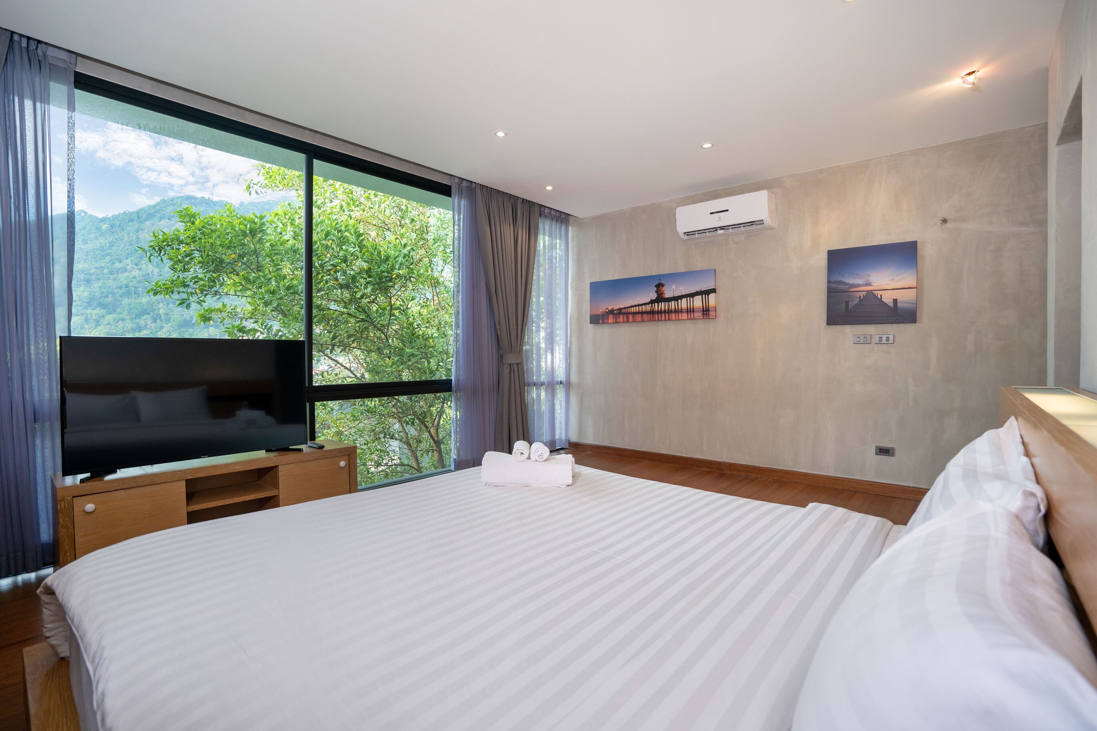 Quarto de hotel moderno com uma cama grande, uma TV de tela plana e uma vista panorâmica de montanhas por grandes janelas.