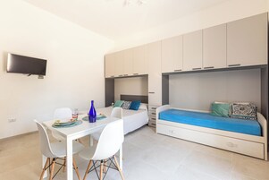 Quarto compacto com cama, escrivaninha e televisão.