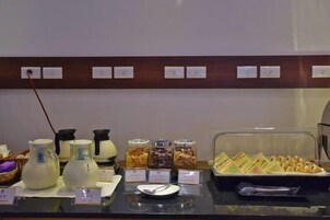 Balcão de buffet com diversos alimentos, incluindo potes de legumes em conserva, uma bandeja de sanduíches e um jarro de leite.