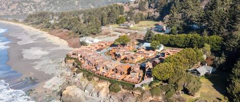 Um resort costeiro com edifícios em terraços, uma praia e colinas arborizadas ao fundo.