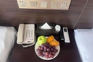 Quarto de hotel com mesa de cabeceira contendo telefone, caixa de lenços, controle remoto e uma travessa de frutas.