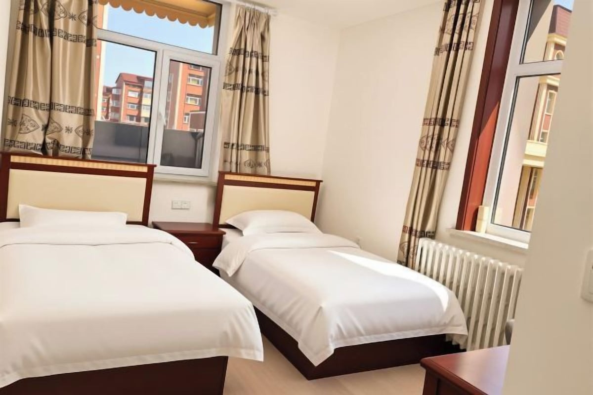 Quarto de hotel com duas camas, janela com cortinas e vista para edifícios.