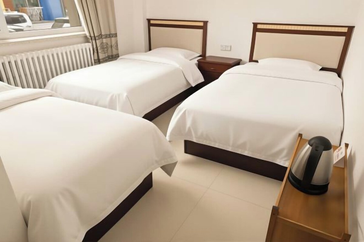 Quarto de hotel com duas camas de solteiro, uma mesa de cabeceira com chaleira e janela com vista para a rua.