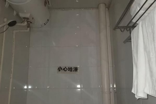 Área de chuveiro com azulejos, um aviso, um porta-toalhas e um chuveiro.